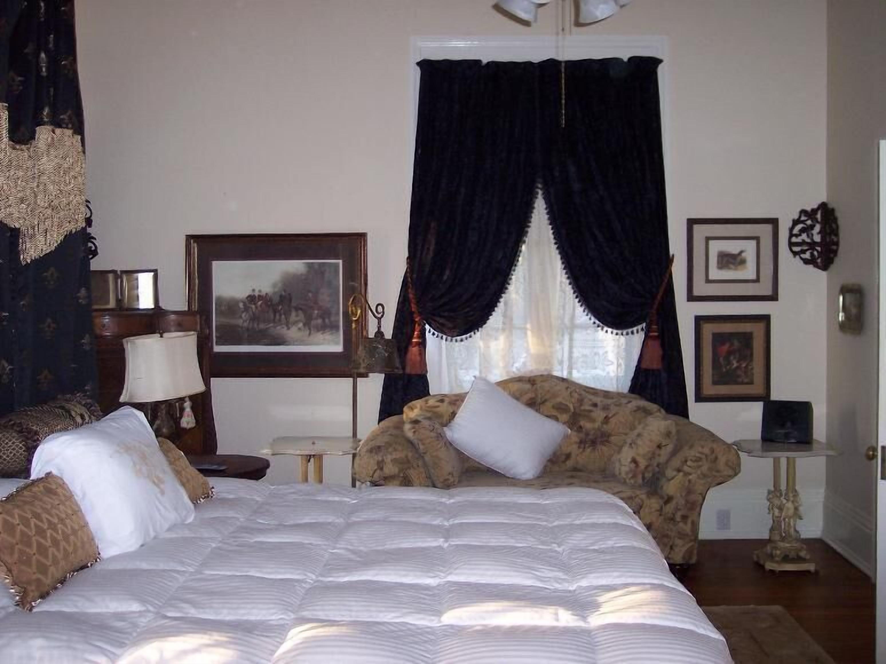 Quarto com cama grande, uma cadeira, luminária e um quadro na parede.