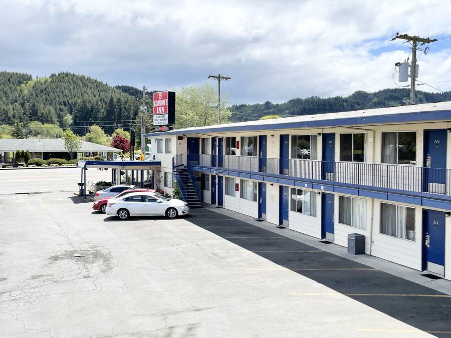 Um motel com estrutura em dois andares, área de estacionamento coberta e placa anunciando política de quartos limpos.