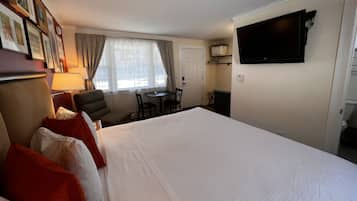 Quarto de hotel com uma cama grande, uma escrivaninha com duas cadeiras, uma televisão fixada na parede e quadros enquadrados.