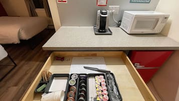 Uma cozinha compacta com cafeteira, micro-ondas e uma gaveta com utensílios e lanches.
