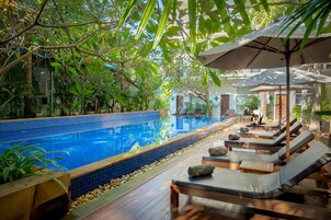 Uma área de piscina com espreguiçadeiras e guarda-sóis, rodeada por vegetação exuberante.
