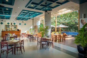 Amplo espaço interno com diversas mesas e cadeiras para refeições, área de bar com variedade de garrafas, e vista para uma área de piscina com guarda-sóis.
