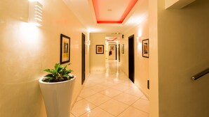 Um corredor de hotel com piso ladrilhado, quadros nas paredes e um vaso de planta.