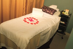 Cama bem arrumada com um arranjo de pétalas de rosas em formato de coração e uma única flor rosa.