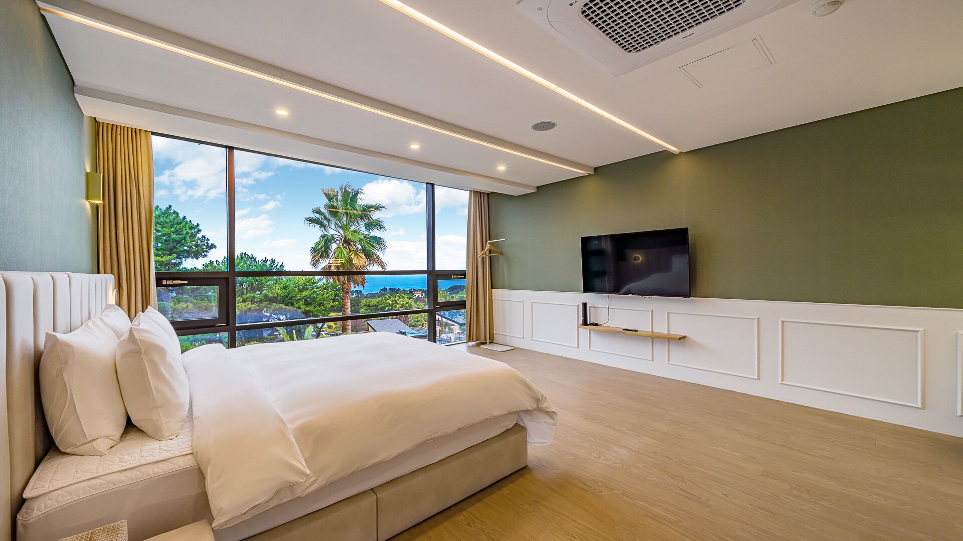 Quarto moderno com uma cama grande, televisão na parede e vista para o exterior.