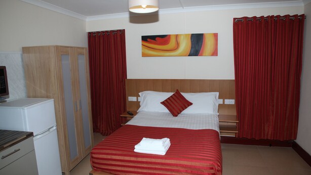 Quarto de hotel com cama, escrivaninha, guarda-roupa e um quadro na parede.