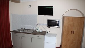 Cozinha compacta com pia, micro-ondas e uma pequena geladeira. Há um armário de madeira e uma cortina vermelha.