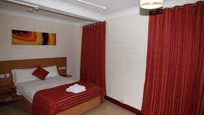 Quarto de hotel com cama, mesa de cabeceira, cortina vermelha e um quadro na parede.