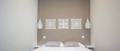 Cama bem arrumada com manta marrom, dois travesseiros e três painéis decorativos fixados na parede.