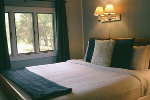 Quarto de hotel com cama, duas luminárias na parede e janela com cortinas.