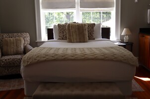 Quarto com uma cama grande, uma cadeira com almofada de estampa de leopardo e janela com vista para árvores.