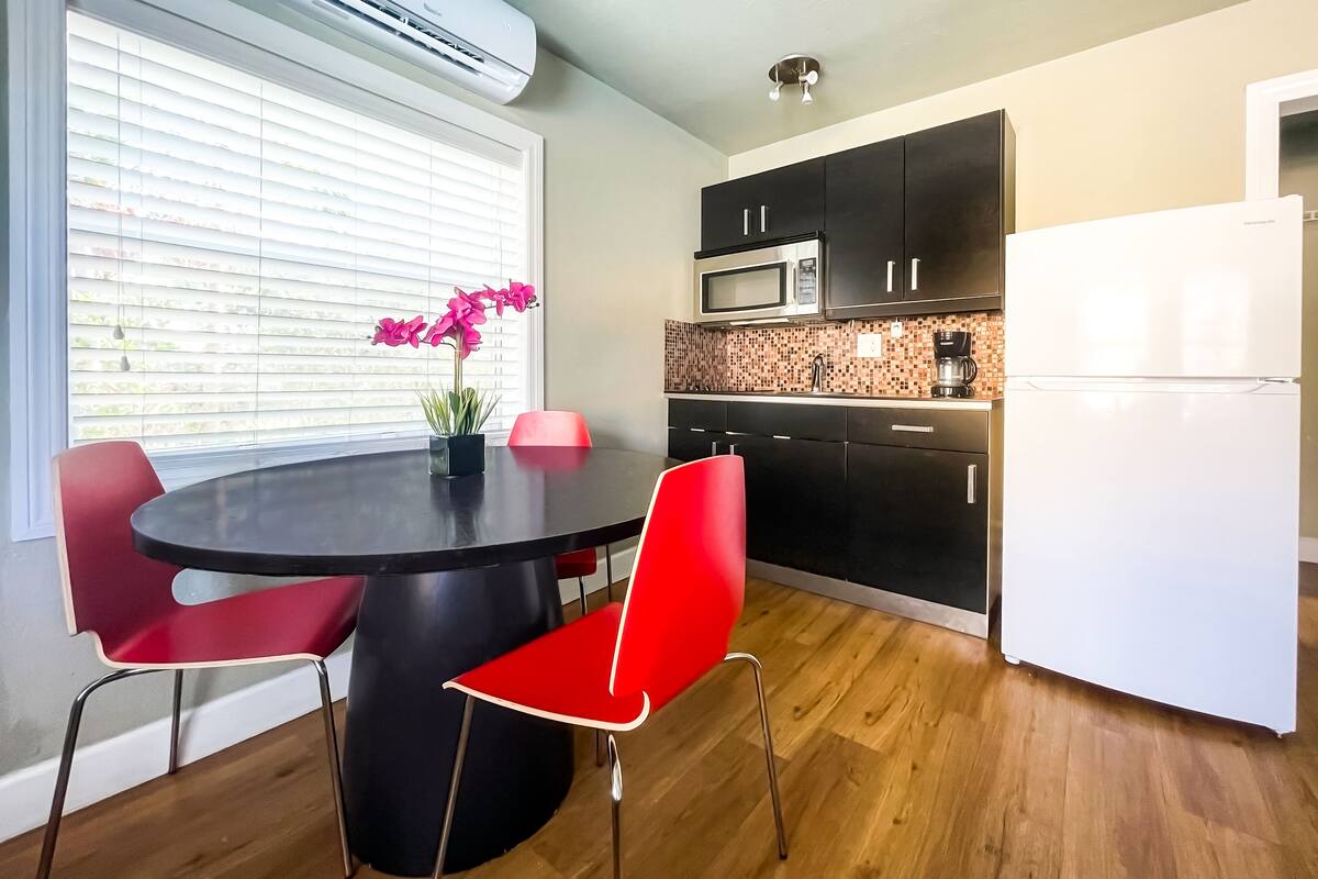 Cozinha moderna com armários pretos, geladeira branca e mesa redonda com cadeiras vermelhas.