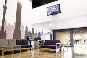 Um hall de entrada com balcão de recepção, área de estar com sofás, uma tela grande e um mural com vista para a cidade na parede.