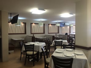 Um restaurante com várias mesas e cabines, cada uma com toalhas brancas e pratos postos.