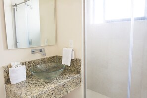 Casa de banho com lavatório de vidro, espelho e chuveiro.