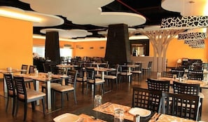 Um restaurante espaçoso com várias mesas e cadeiras, design de teto moderno e uma estrutura decorativa central.