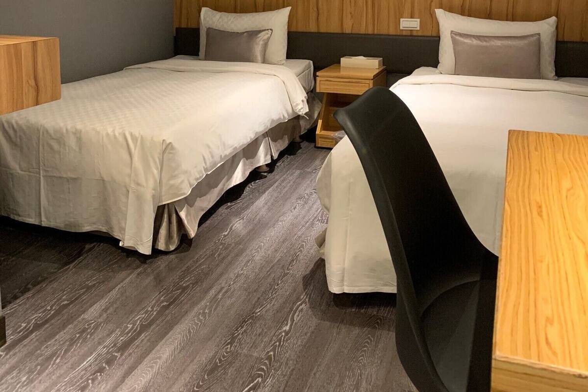 Quarto de hotel com duas camas, uma cabeceira de madeira, uma mesinha de cabeceira pequena de madeira e uma cadeira.