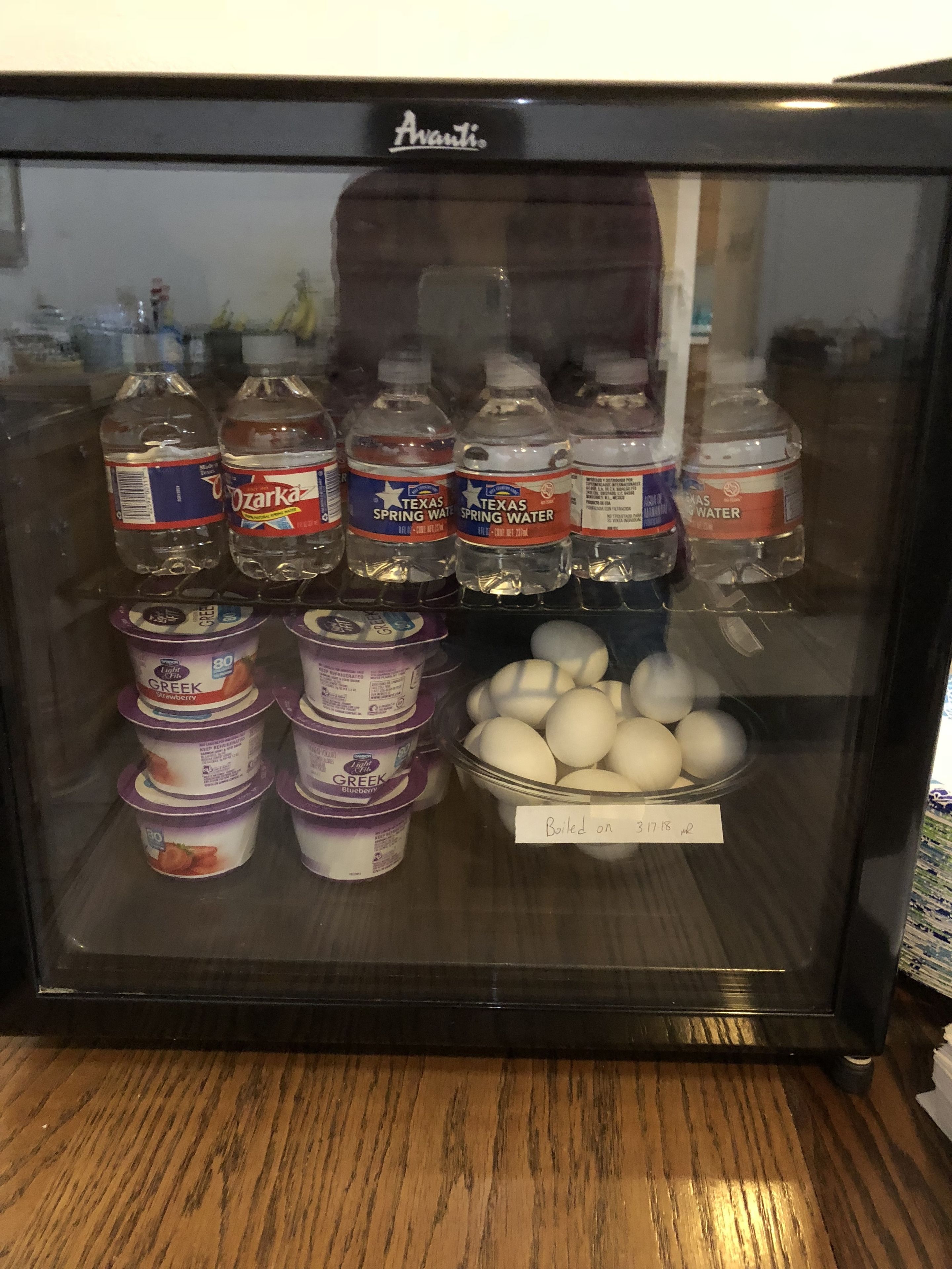 Uma geladeira com água engarrafada, iogurte e ovos.