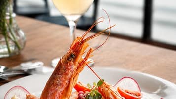 Prato de frutos do mar com camarões e vieiras, acompanhado de um copo de vinho branco e um arranjo floral.