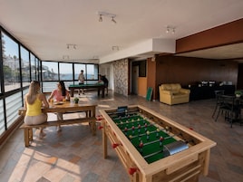 Um espaço amplo e interno com mesa de pebolim, mesa de bilhar e área de estar com vista para o exterior.