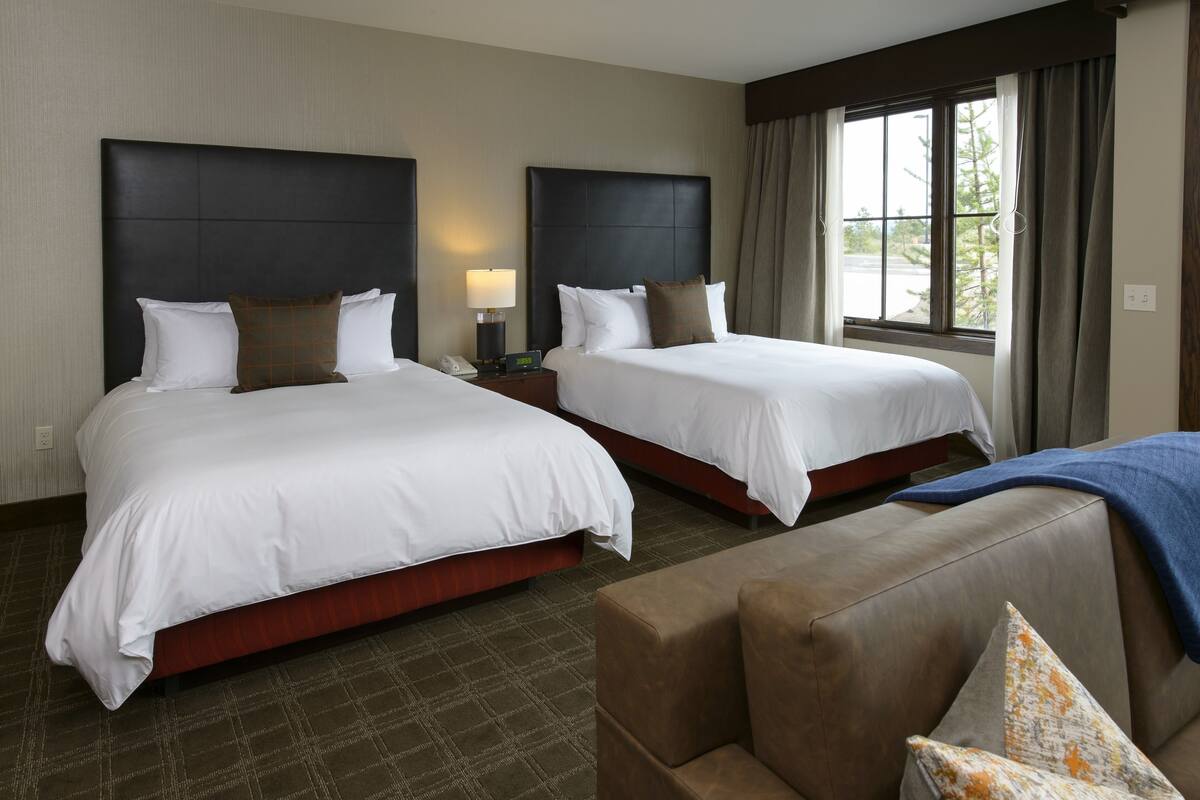 Quarto de hotel com duas camas, um sofá e uma janela com cortinas.