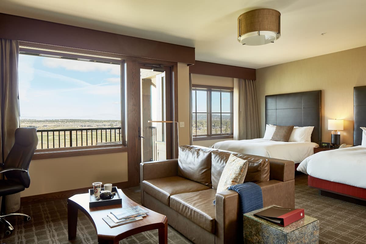 Quarto de hotel com uma grande janela, um sofá, uma escrivaninha e duas camas.