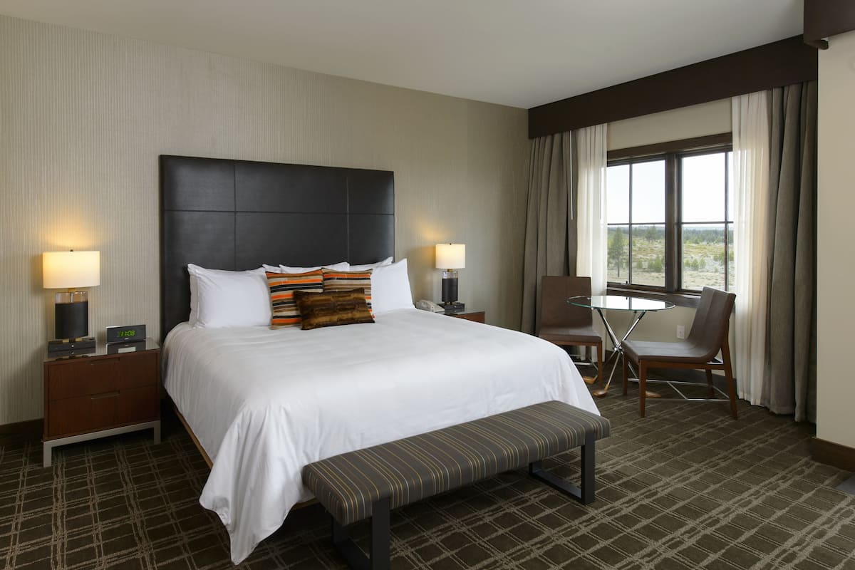 Quarto de hotel com uma cama grande, um banco, uma escrivaninha e uma cadeira.