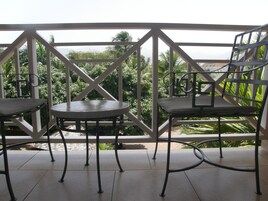 Varanda com duas cadeiras e uma mesa, rodeada por um guarda-corpo branco, com vista para uma paisagem verde exuberante.