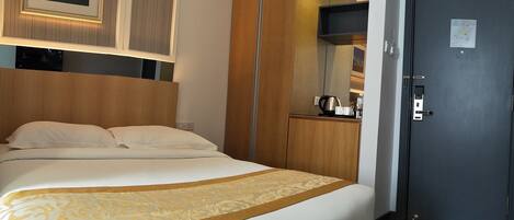 Quarto de hotel com uma cama grande, guarda-roupa de madeira, uma kitchenette pequena e uma porta com um mapa.