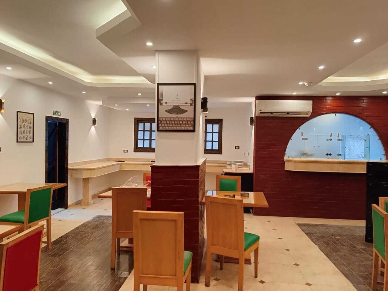 Um interior moderno com mesas e cadeiras de madeira, uma escadaria central e uma ampla janela em arco.