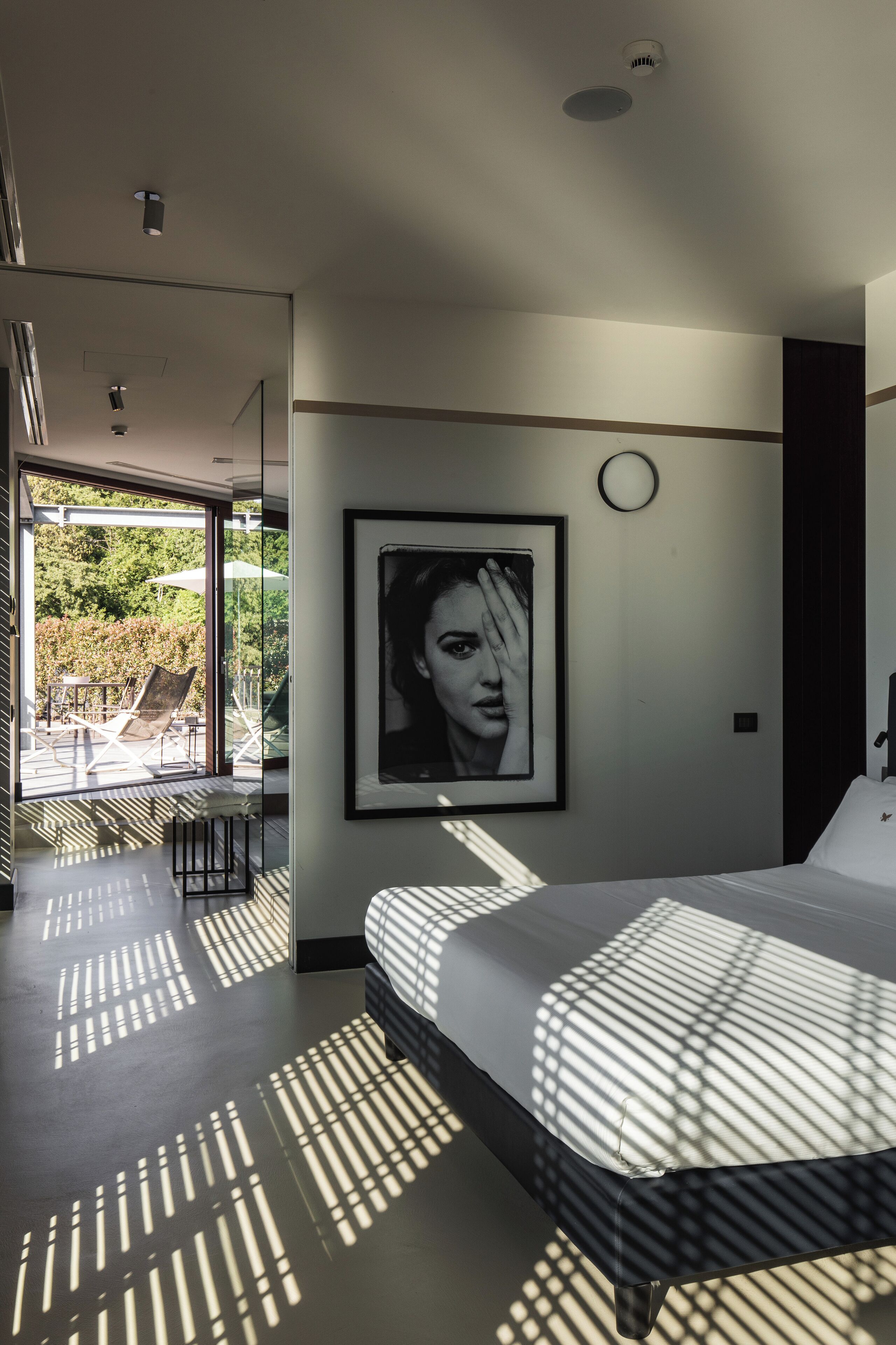Quarto de hotel moderno com uma cama grande, um retrato emoldurado na parede e vista para o exterior através de uma porta de vidro.