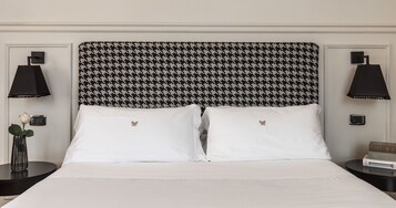 Cama com roupa de cama branca, cabeceira estampada em xadrez houndstooth e duas luminárias de cabeceira.