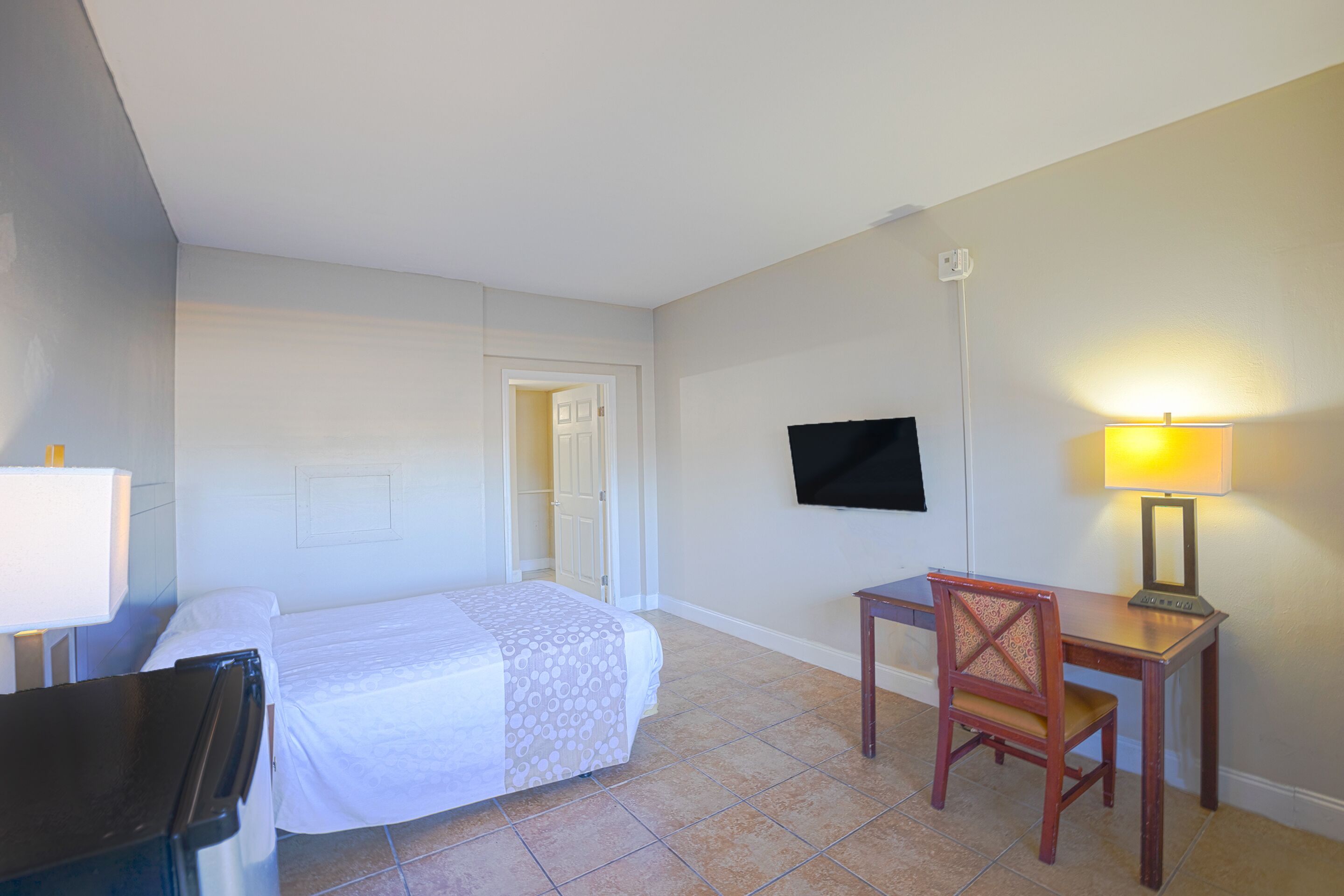 Quarto de hotel com cama, escrivaninha, cadeira, televisão e abajur.