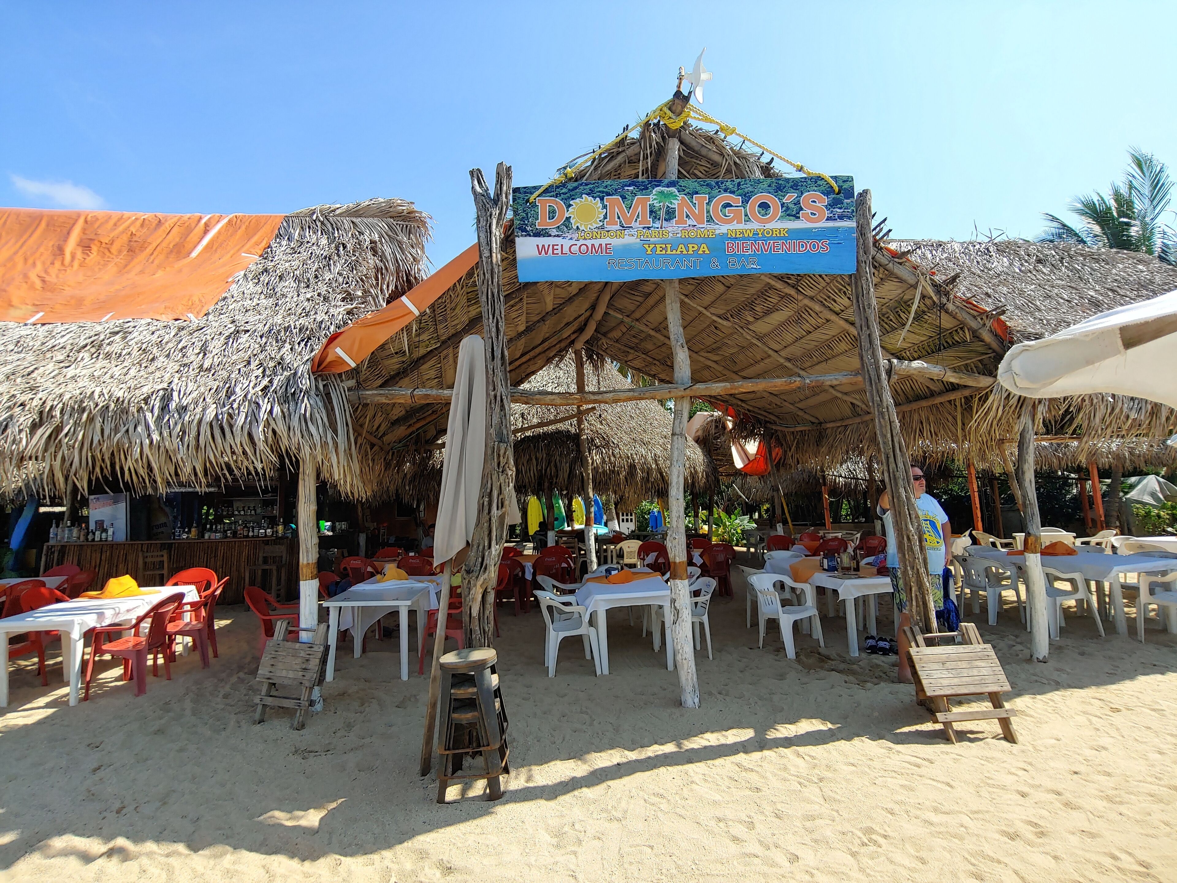 Um restaurante à beira-mar com telhado de palha e mesas ao ar livre.