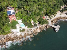 Vista aérea de uma propriedade costeira com piscina, um píer e um edifício com painéis solares.