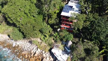 Uma propriedade costeira com um edifício vermelho, painéis solares e uma linha costeira rochosa.