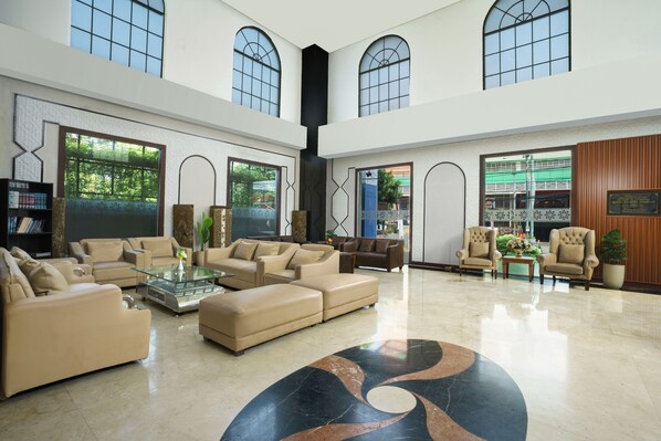 Um hall espaçoso com pé direito alto, janelas amplas e área de estar central com sofás e uma mesa de centro.