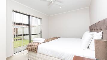 Quarto com cama, ventilador de teto e vista para um quintal através de uma porta de correr.