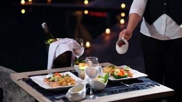 Uma mesa posta com pratos de comida, uma garrafa de vinho e copos, com alguém servindo uma bebida.