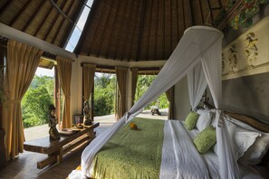 Quarto com cama, um banquinho e vista para o verde lá fora.