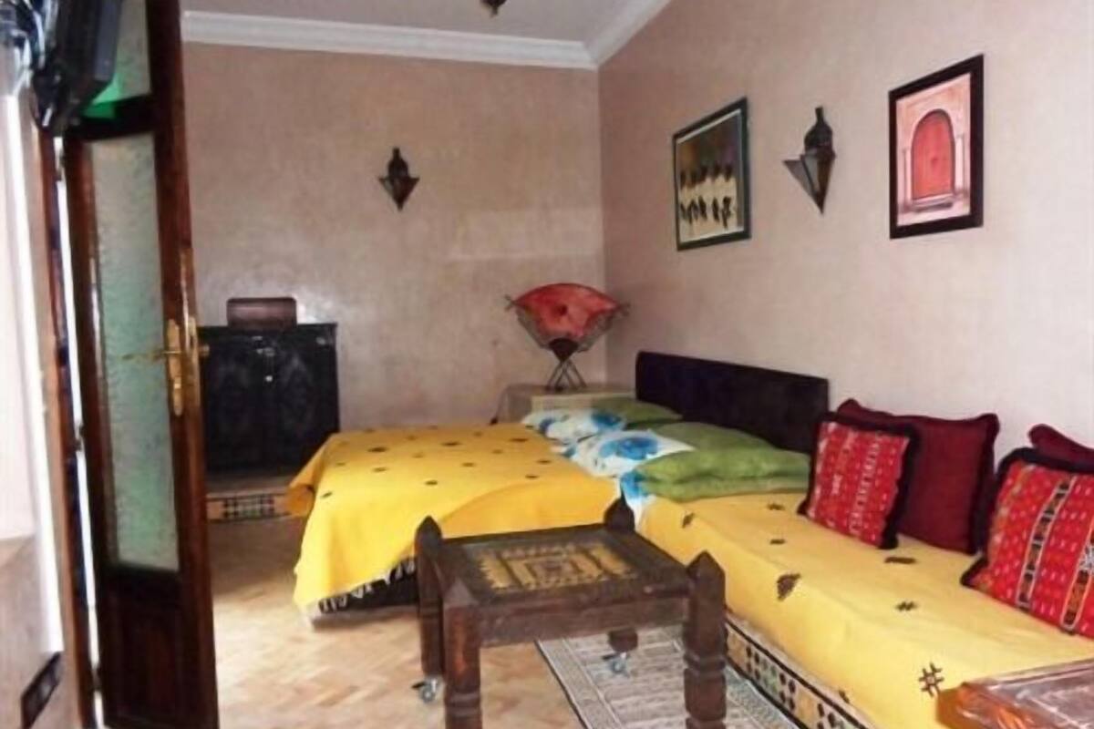 Quarto com uma cama, uma mesa de madeira e um sofá. Há duas luminárias fixadas na parede e um quadro emoldurado.