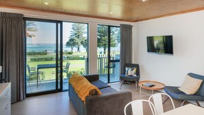 Uma sala de estar moderna com sofá, poltrona, televisão e varanda com vista para o exterior.