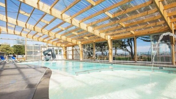 Piscina interna com estrutura de teto de madeira e painéis de vidro transparente.