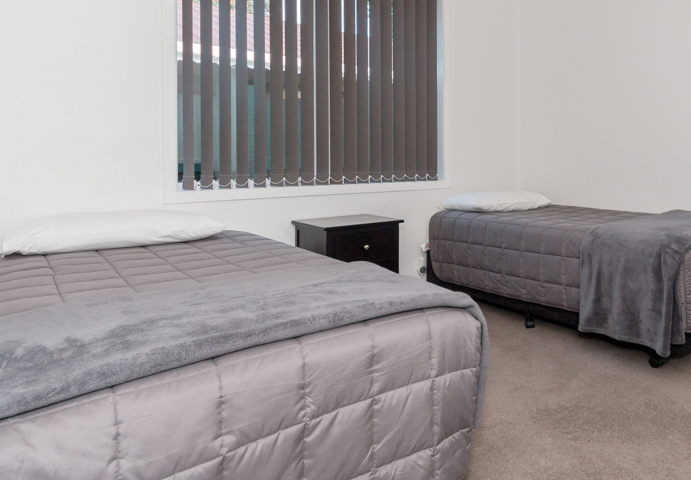 Quarto com duas camas, uma mesa de cabeceira e uma janela com cortinas.