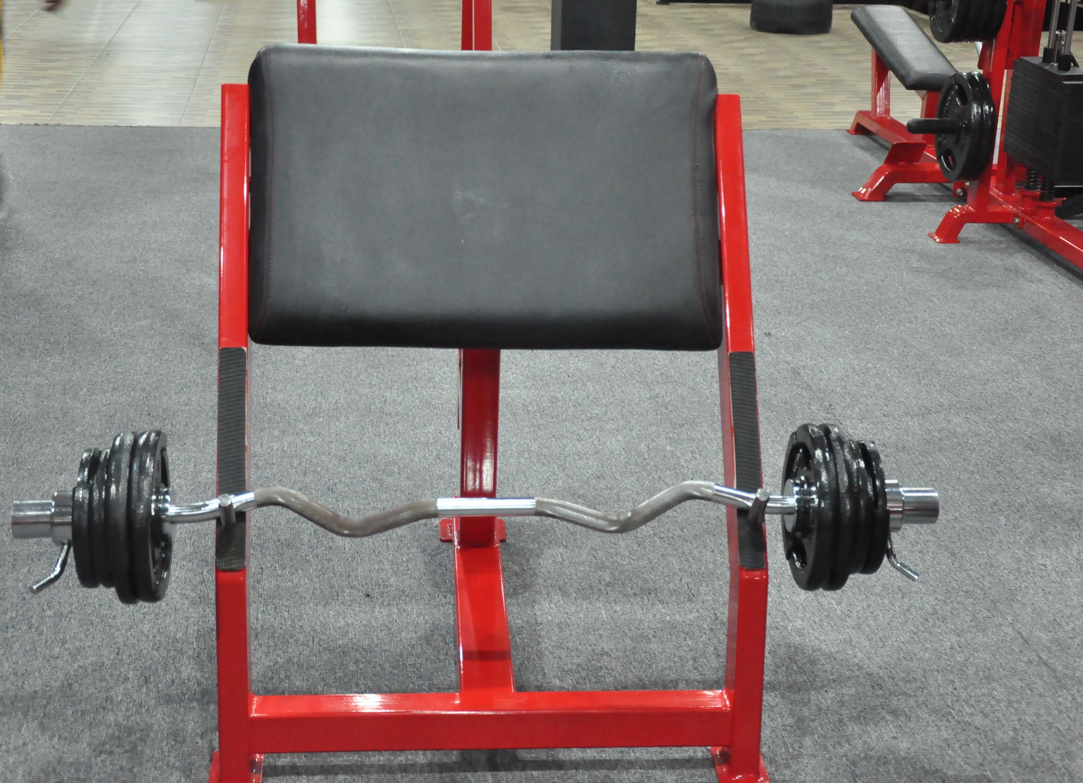 Um banco de musculação vermelho com assento preto e barra com pesos.