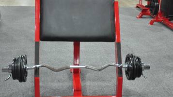 Um banco de musculação vermelho com assento preto e barra com pesos.