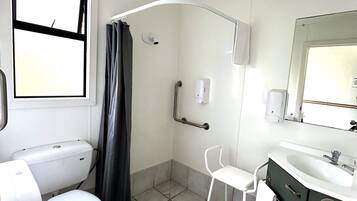 Casa de banho com sanita, chuveiro, lavatório e espelho.