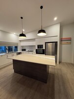 Uma cozinha moderna com ilha central, eletrodomésticos de aço inoxidável e iluminação pendente.