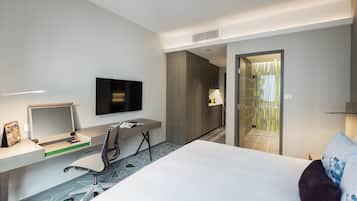 Quarto de hotel moderno com cama, escrivaninha, cadeira, TV e vista para o banheiro.