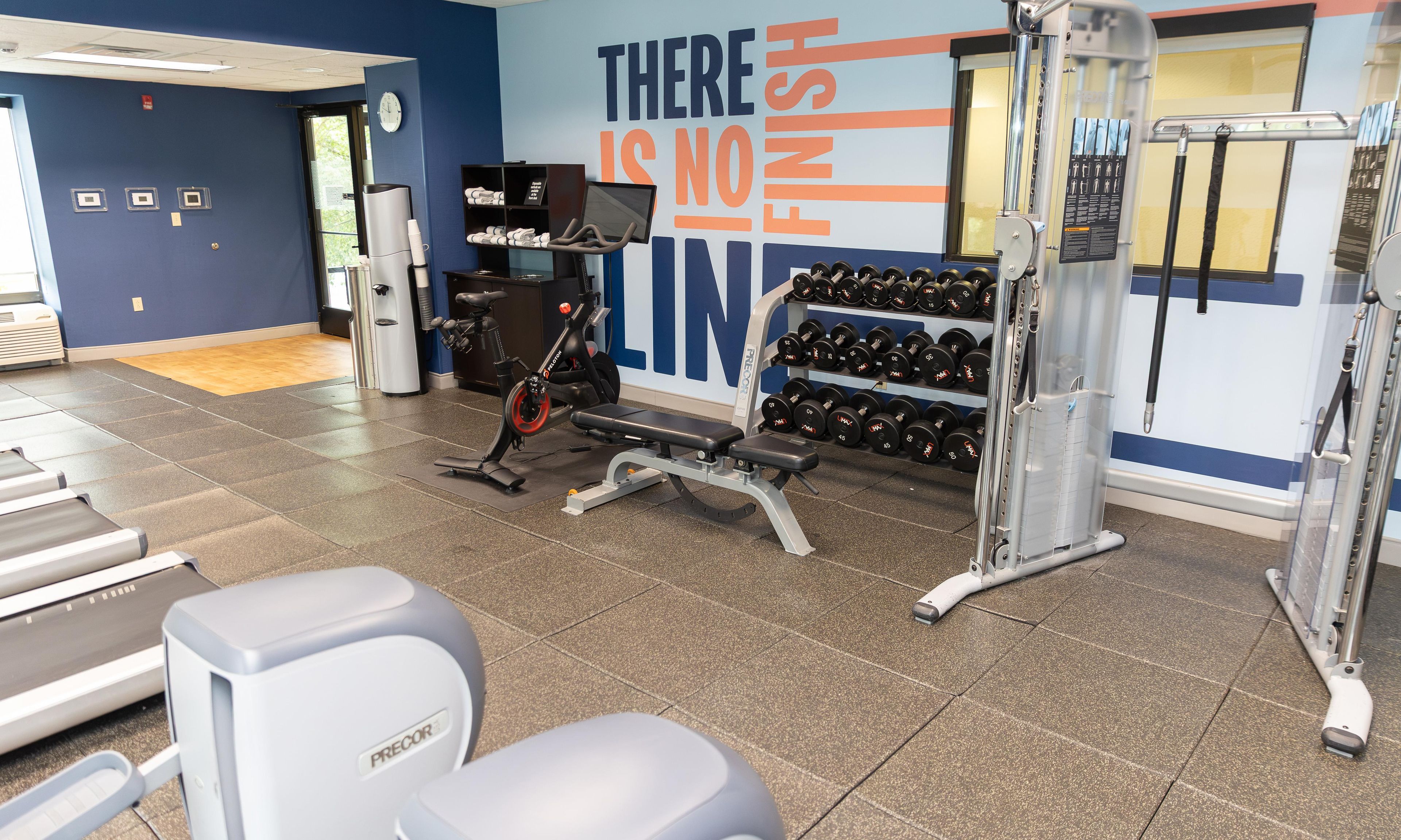 Uma academia com equipamentos de exercício, uma parede com mensagens motivacionais e uma janela.